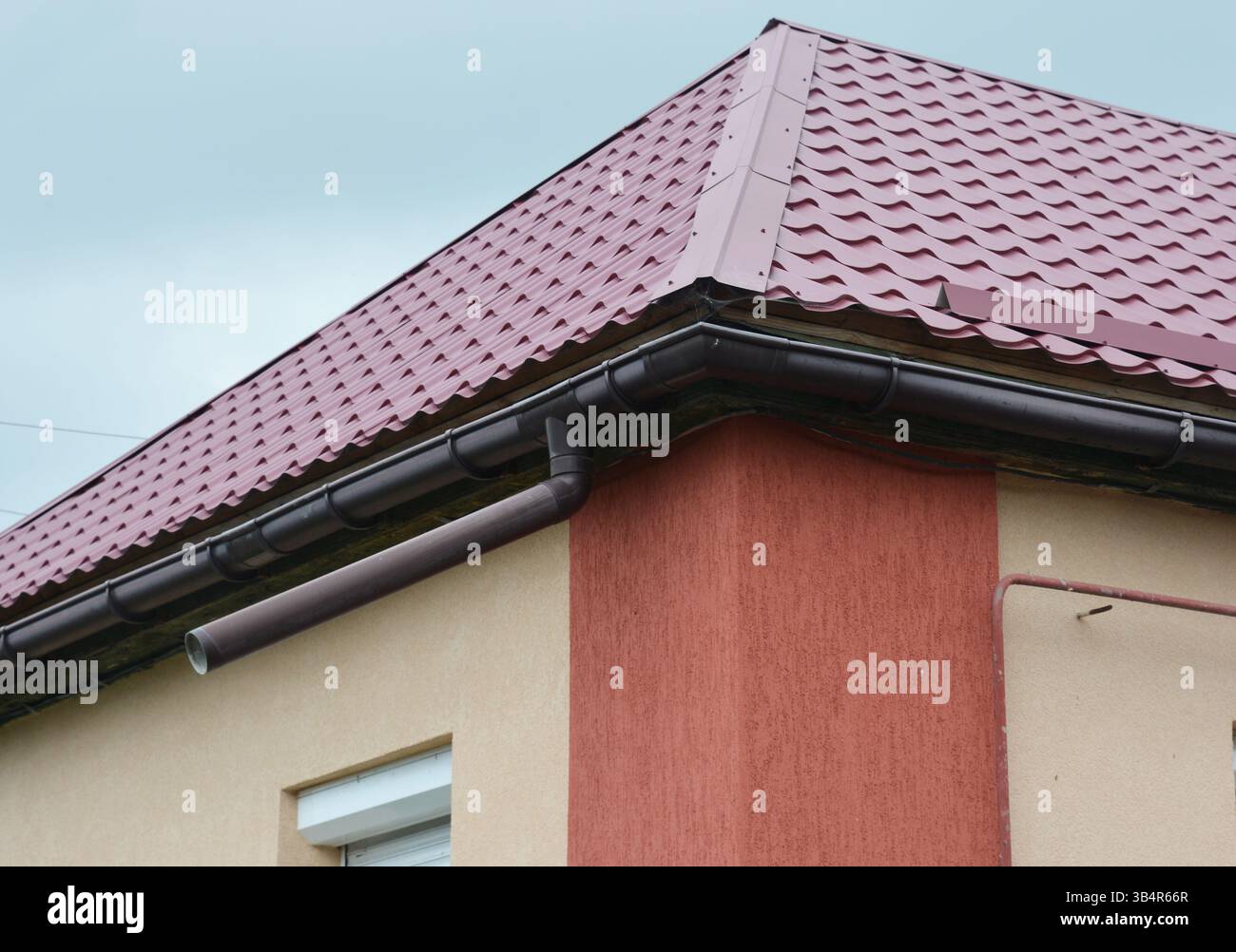 A house with a metal roof and a plastic gutter with a drainage pipe ...