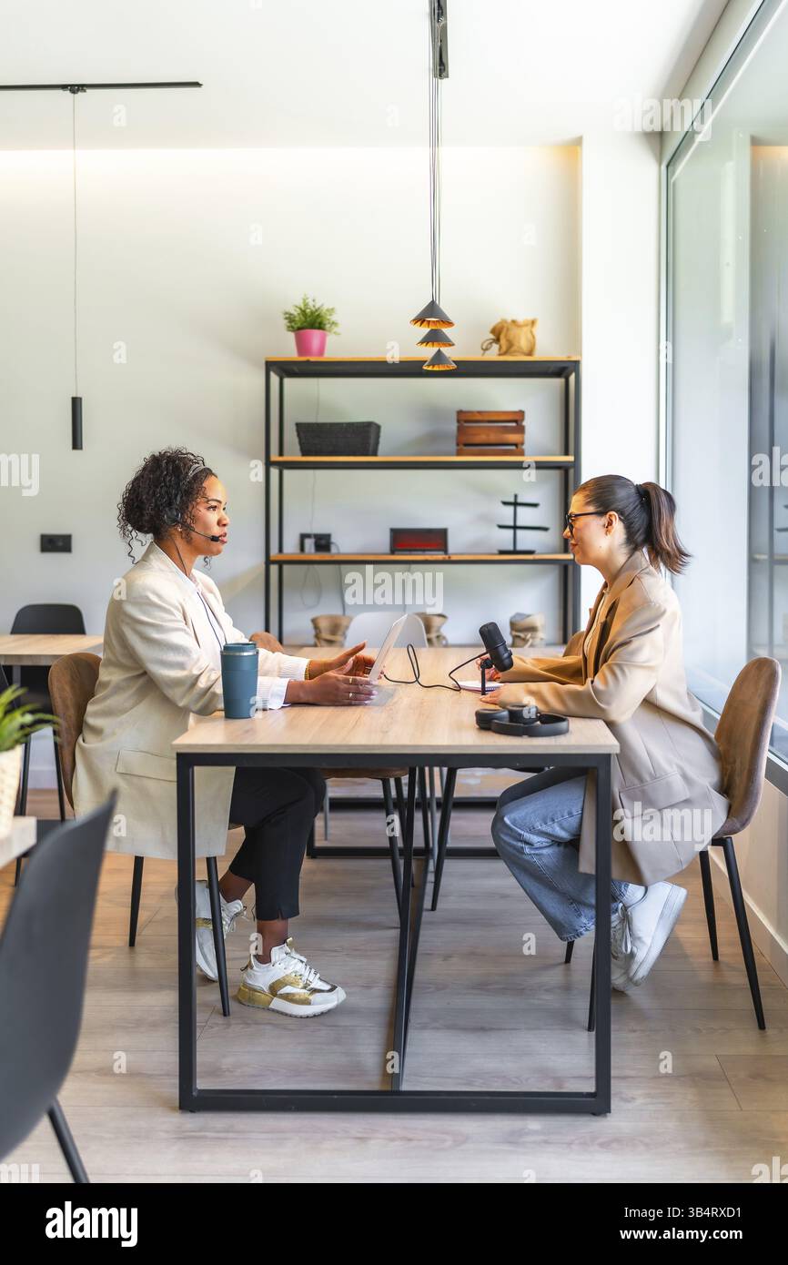 Two businesswomen are recording a podcast in a modern office, using a ...