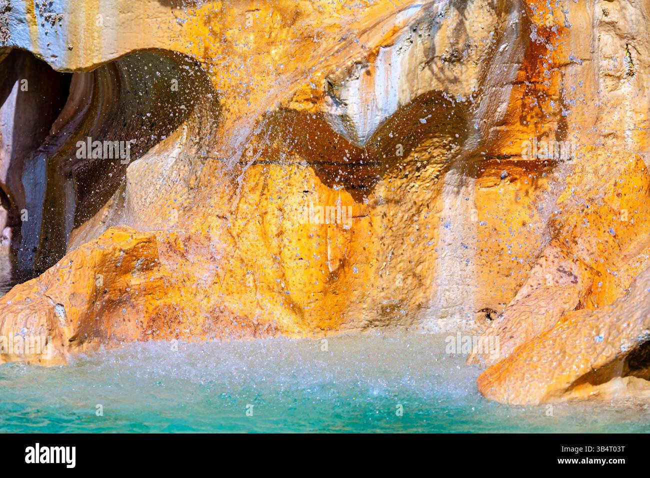 Water cascades from a rugged rock formation into a clear turquoise pool ...