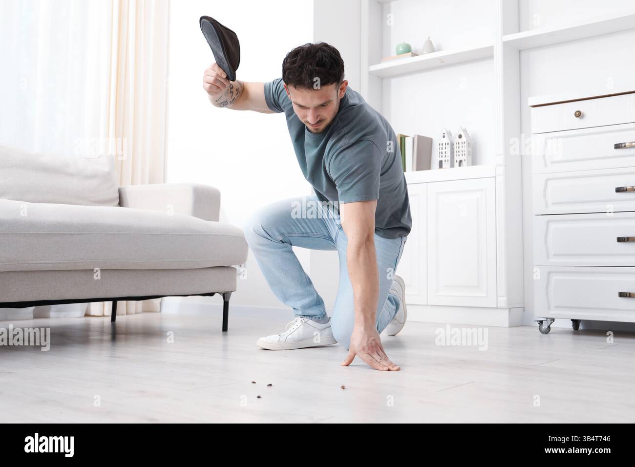 Emotional young man killing cockroaches with slipper on floor indoors ...