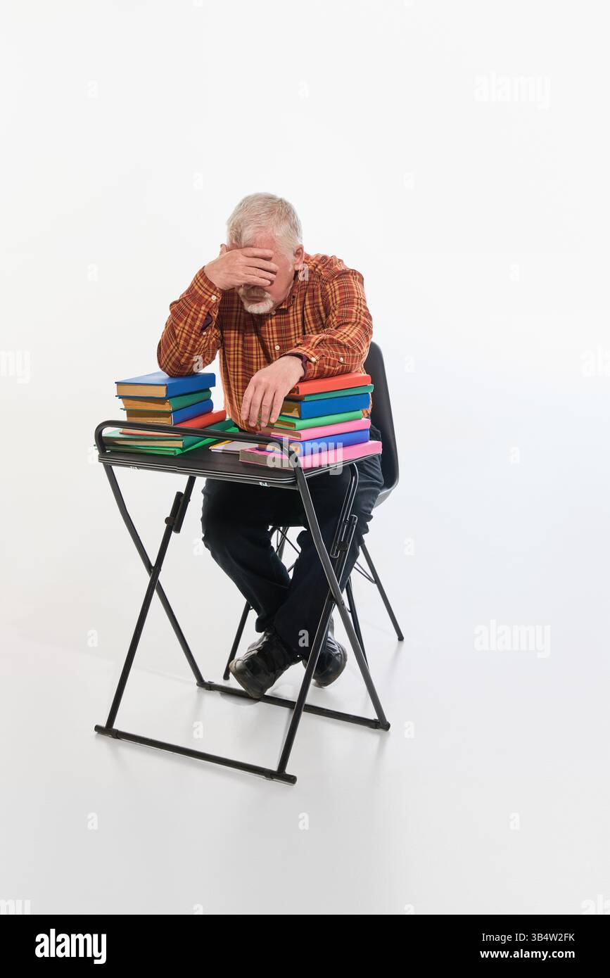 Older man overwhelmed by studies, hand on forehead, sitting with ...