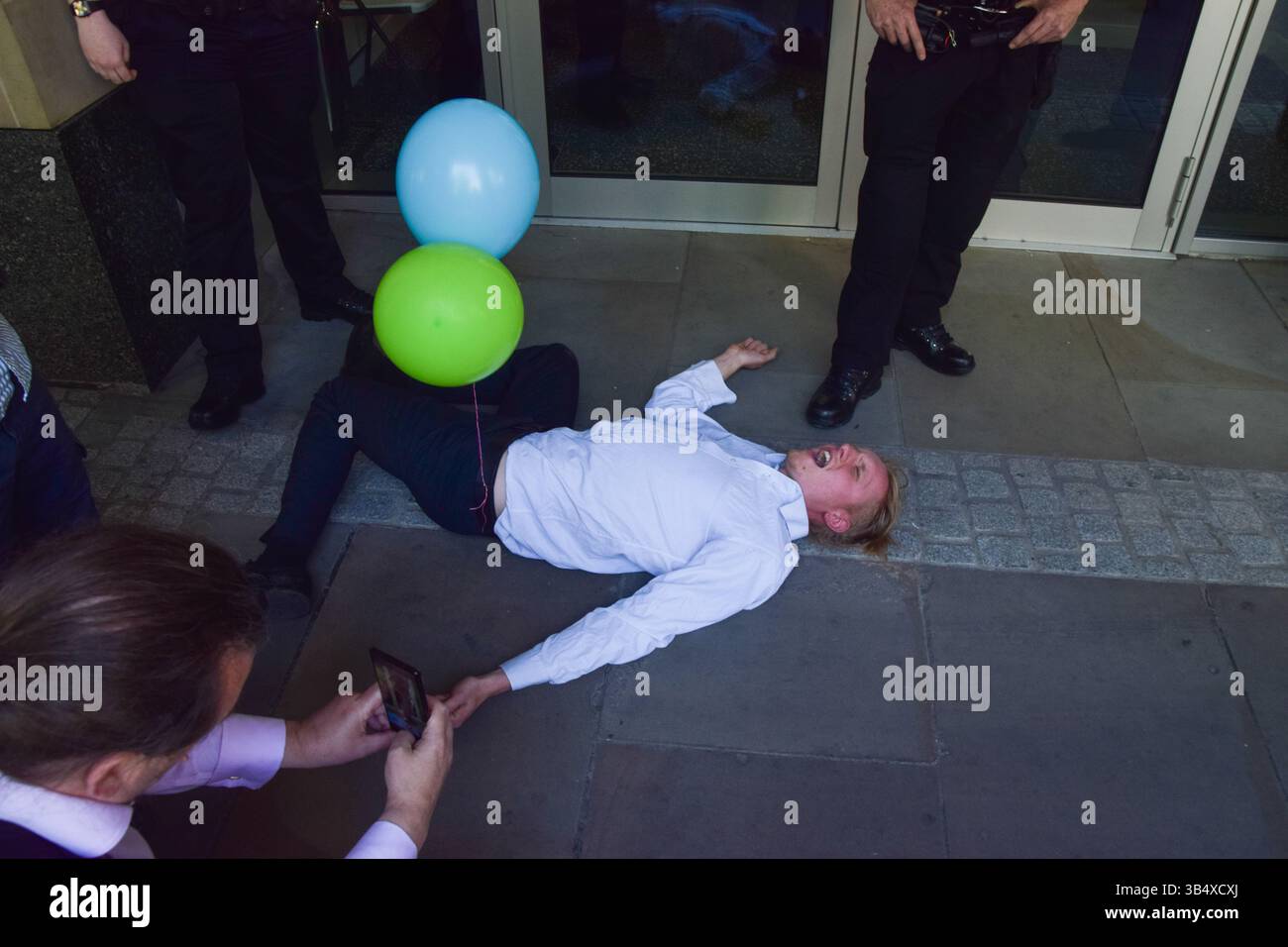 London, UK. 1st May 2025. A protester with balloons lies down outside ...