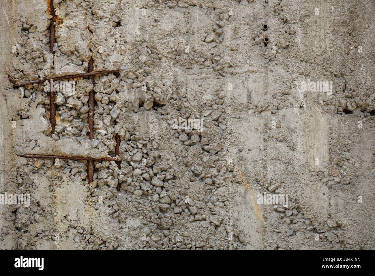 Rusted rebar grid protrudes from unfinished, weathered concrete wall ...