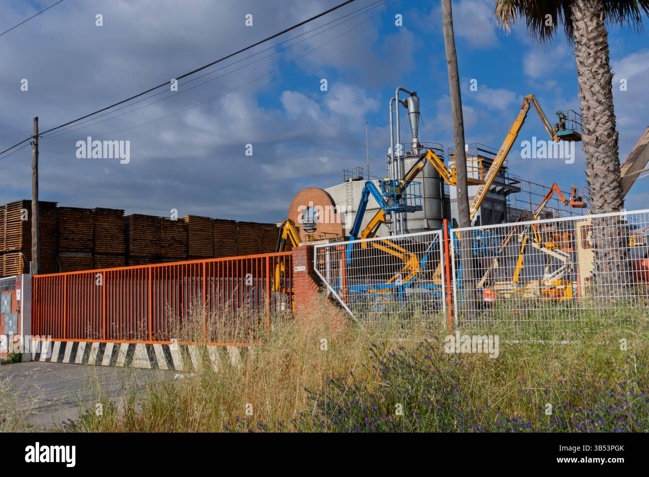 Wooden timber logs piled high near metal perimeter fencing, industrial ...