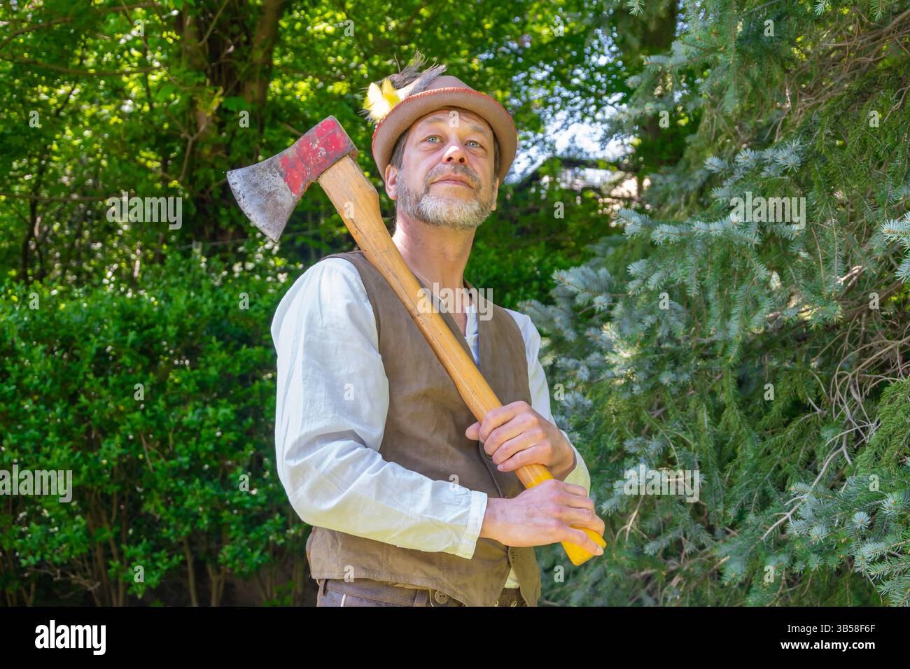 A woodsman with a grey beard and an axe in his hand poses in nature in ...