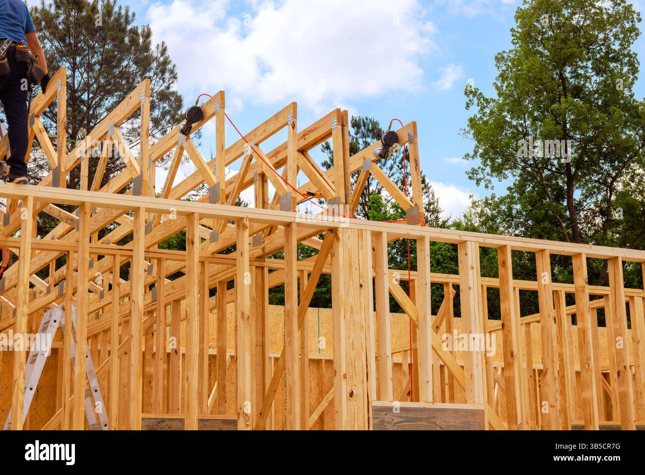 Workers in safety gear are installing wooden trusses on building under ...