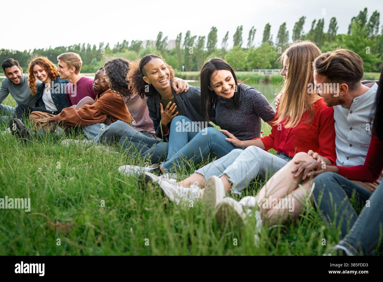 Diverse group of young friends sitting together outdoors, enjoying a ...