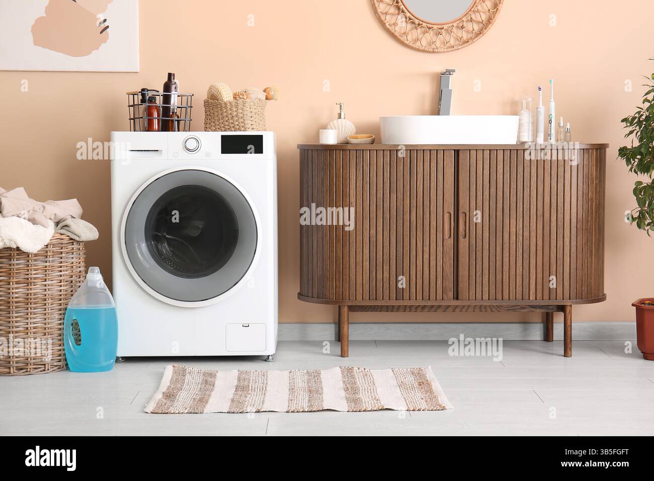 Modern washing machine, basket with laundry and chest of drawers in ...
