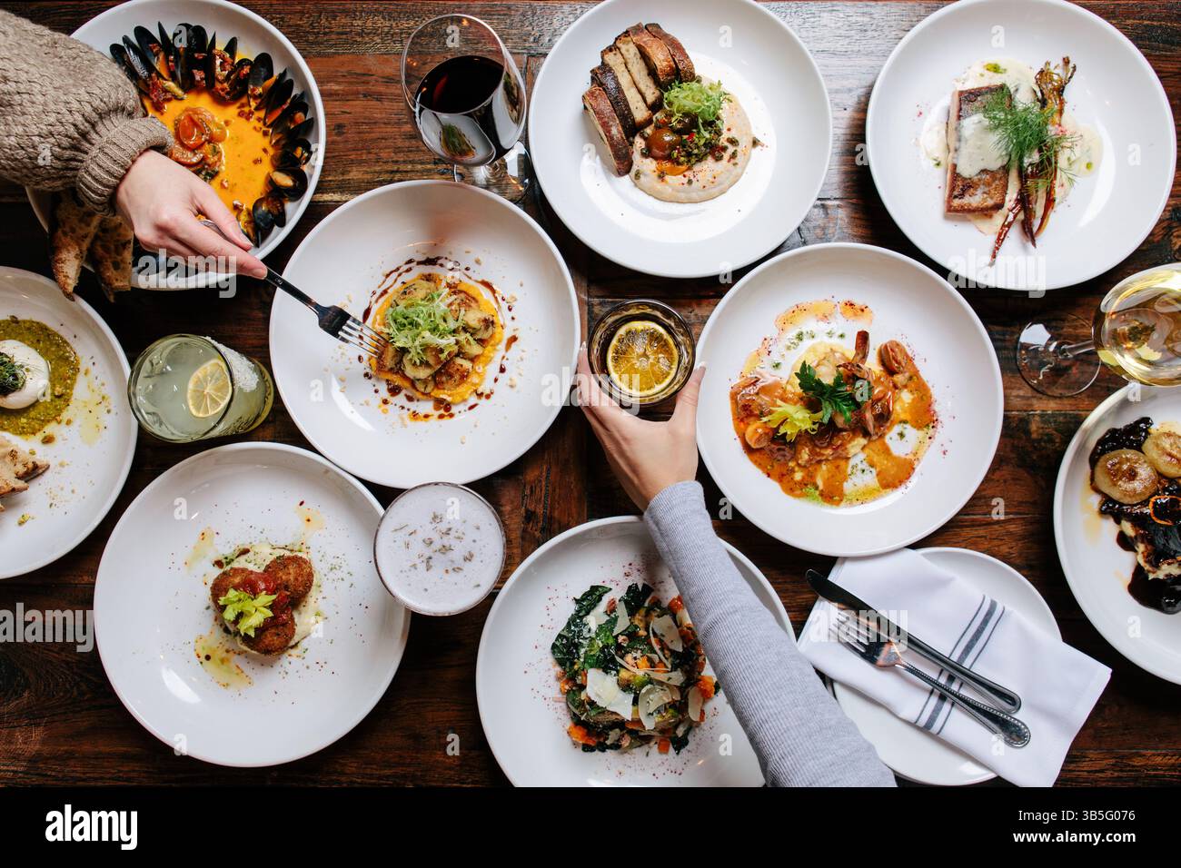Two female hands reaching over tabletop food spread Stock Photo - Alamy