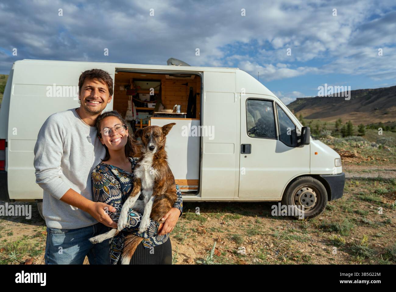 Happy couple with dog hugging in front of camper van Stock Photo - Alamy