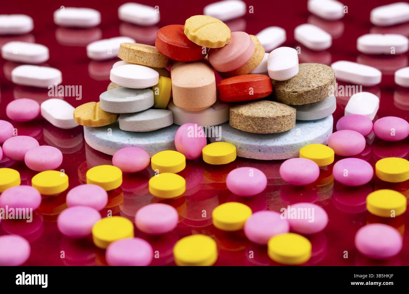 Different colorful pills and capsules isolated on a red reflective ...