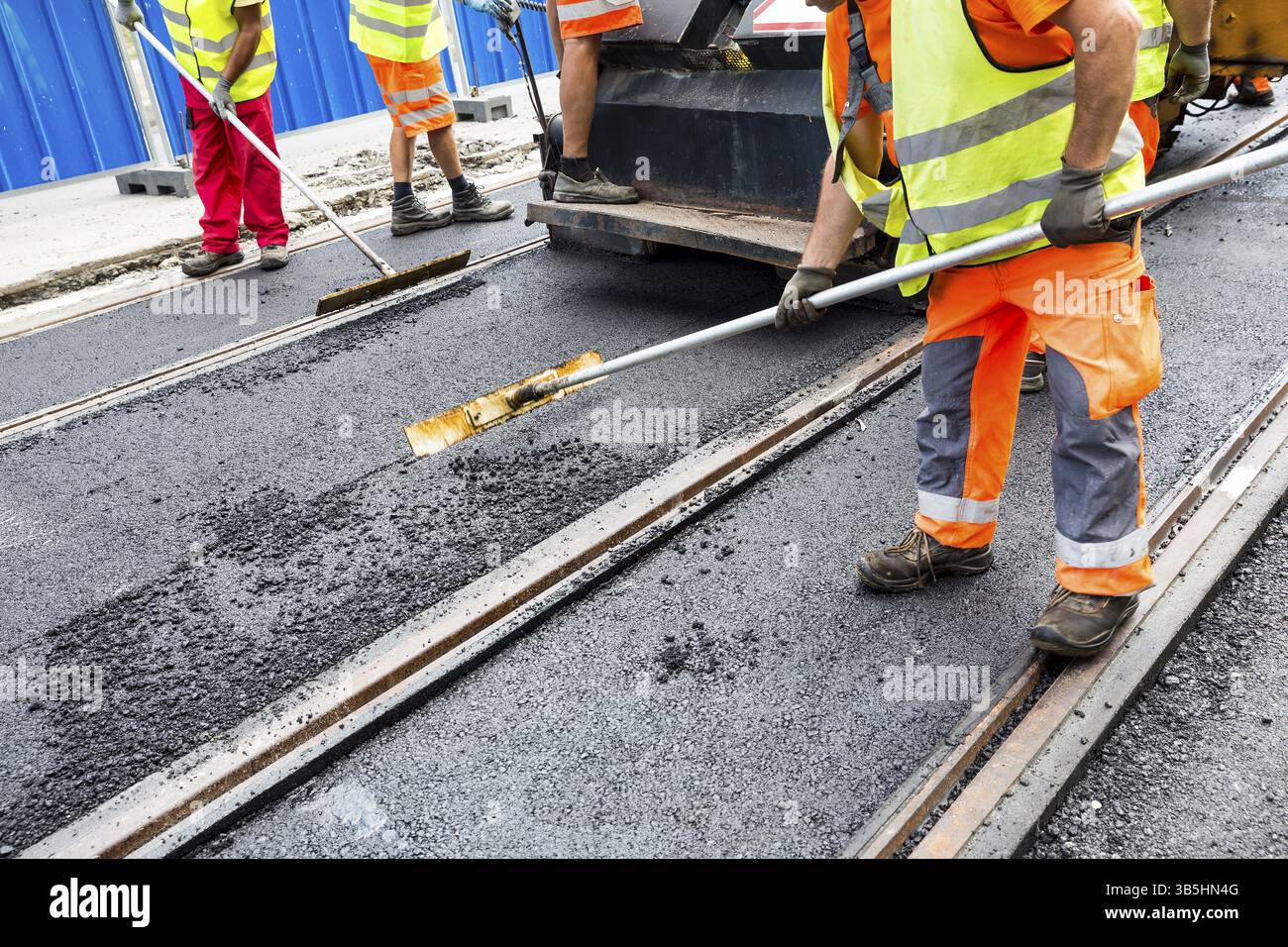 Team of workers put the hot asphalt on a street along tram car's ...