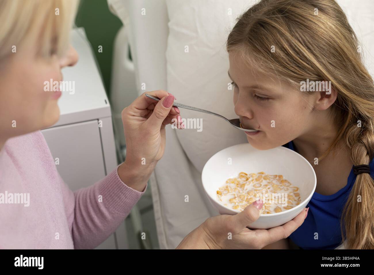 A loving mother helps her daughter eat cereal, showcasing care and ...