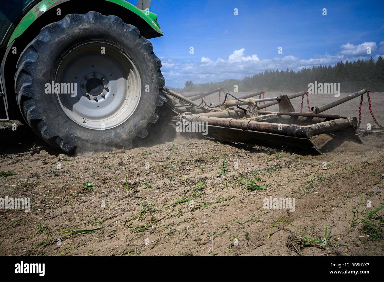 Green tractor pulling a land roller, performing soil leveling and ...
