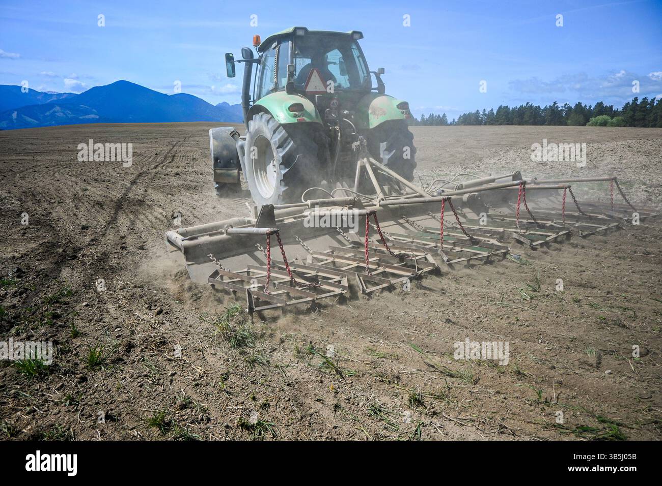 Green tractor pulling a land roller, performing soil leveling and ...