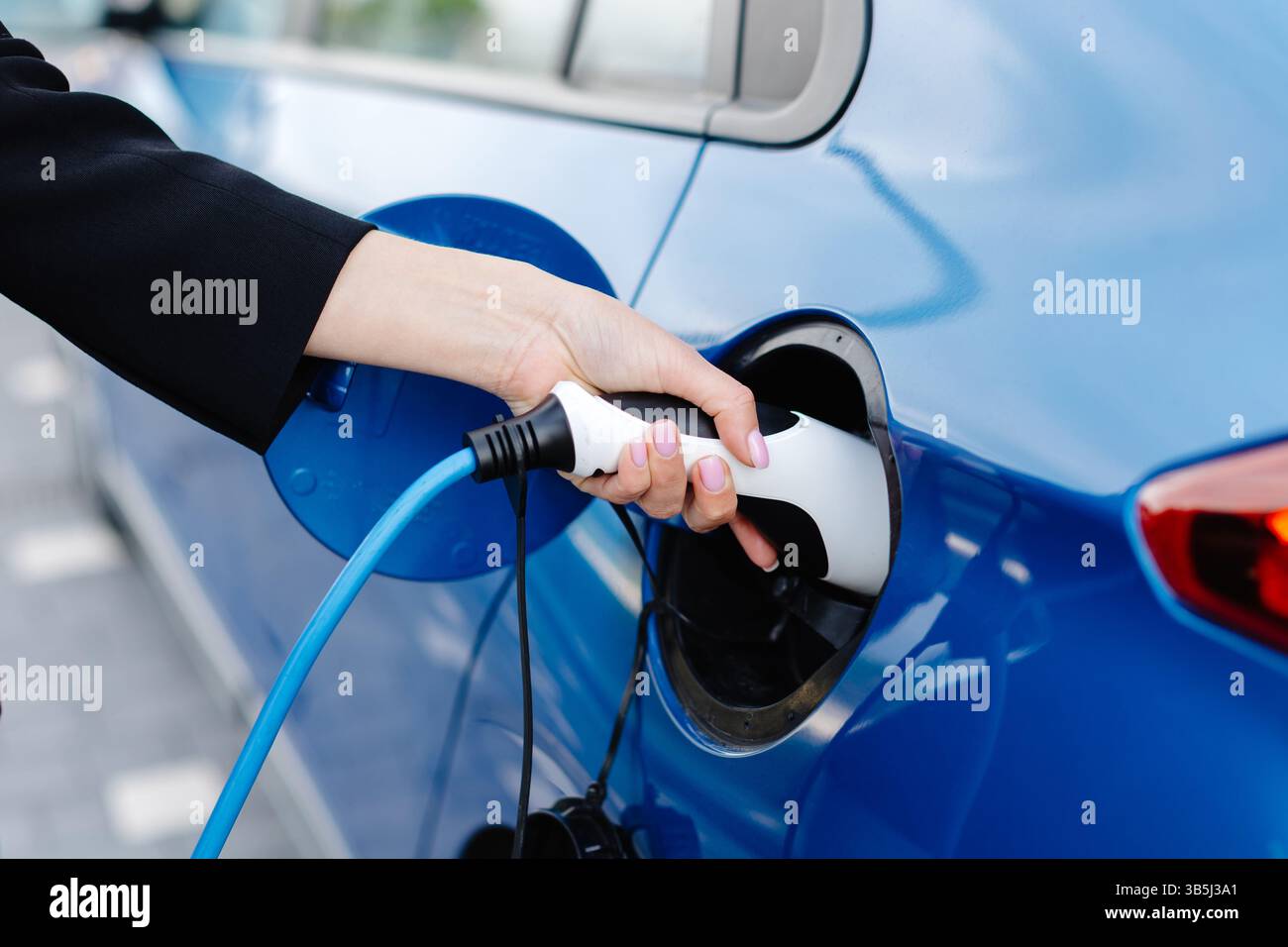 Woman install cable plug to her electric car with home charging station ...