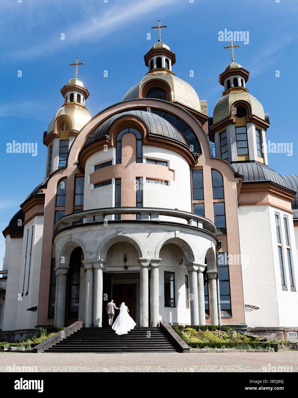 A bride and groom descend the steps of a majestic church, sunlight ...