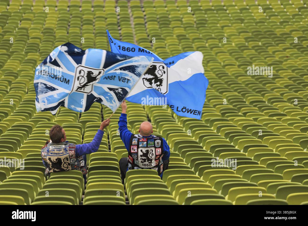 Two football fans waving flags of TSV 1860 Munich in an empty stadium ...