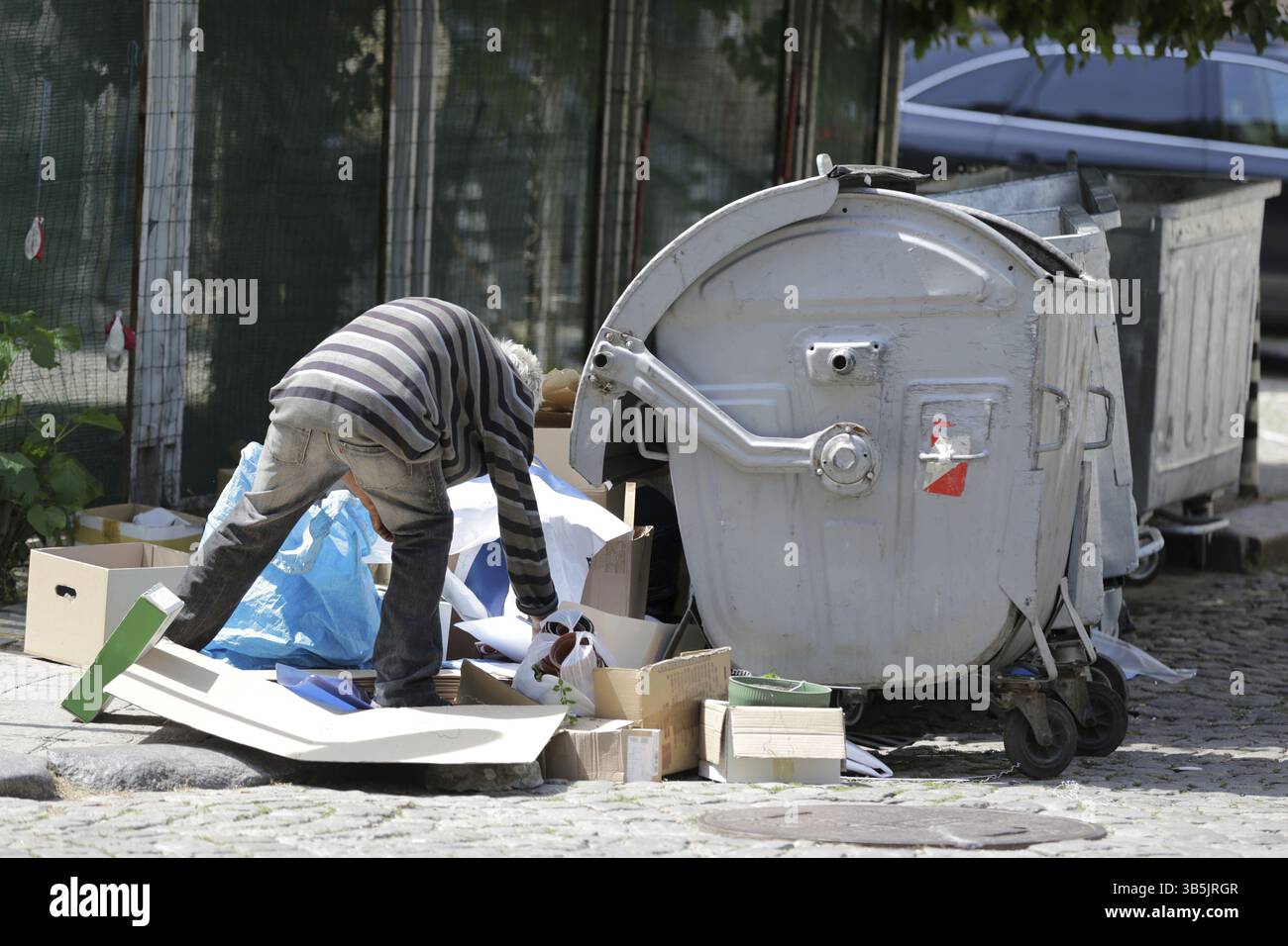 Poor homeless man collects paper near trash bins for recycling in Sofia ...