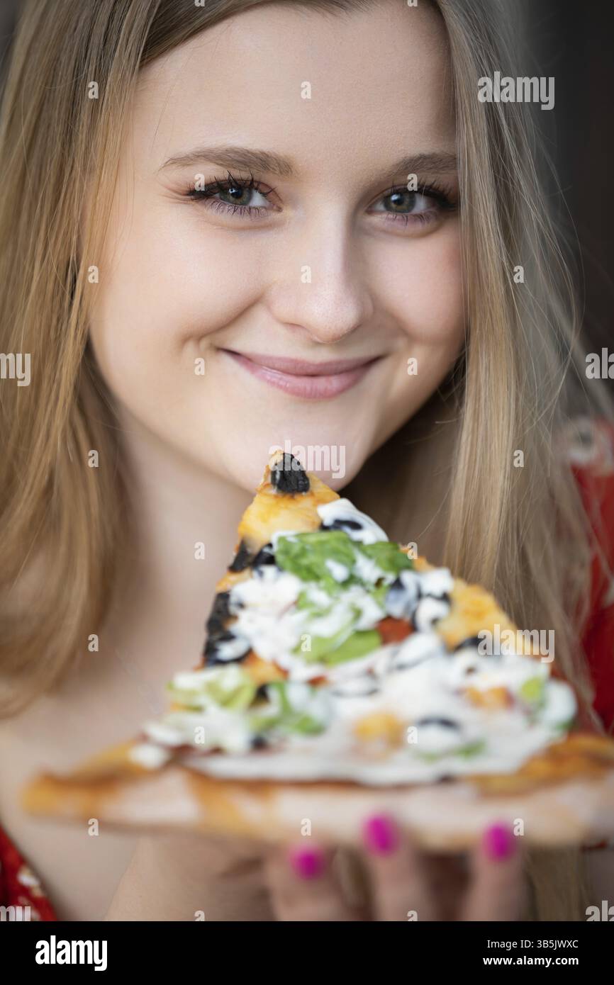 Portrait of a long-haired girl holding a slice of pizza in front of her ...