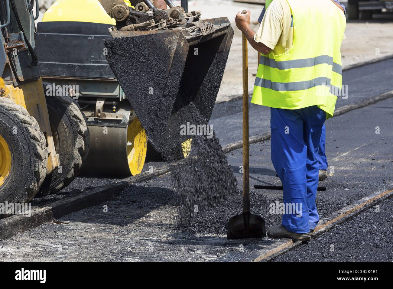 Worker put the hot asphalt on a street along tram car's railroad lines. Road construction ...