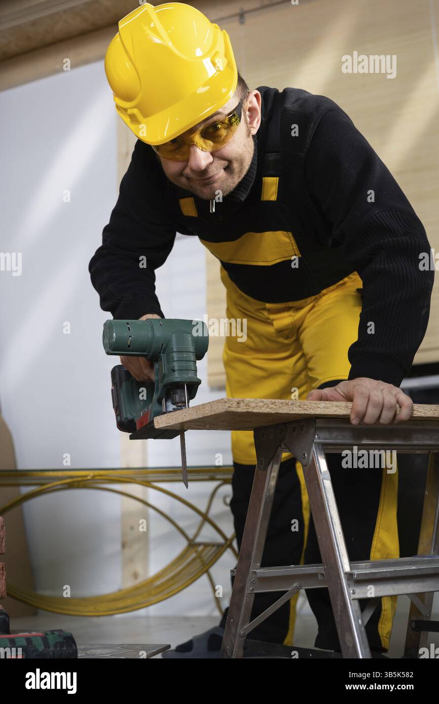 The construction worker cuts the wooden board with an electric jigsaw ...