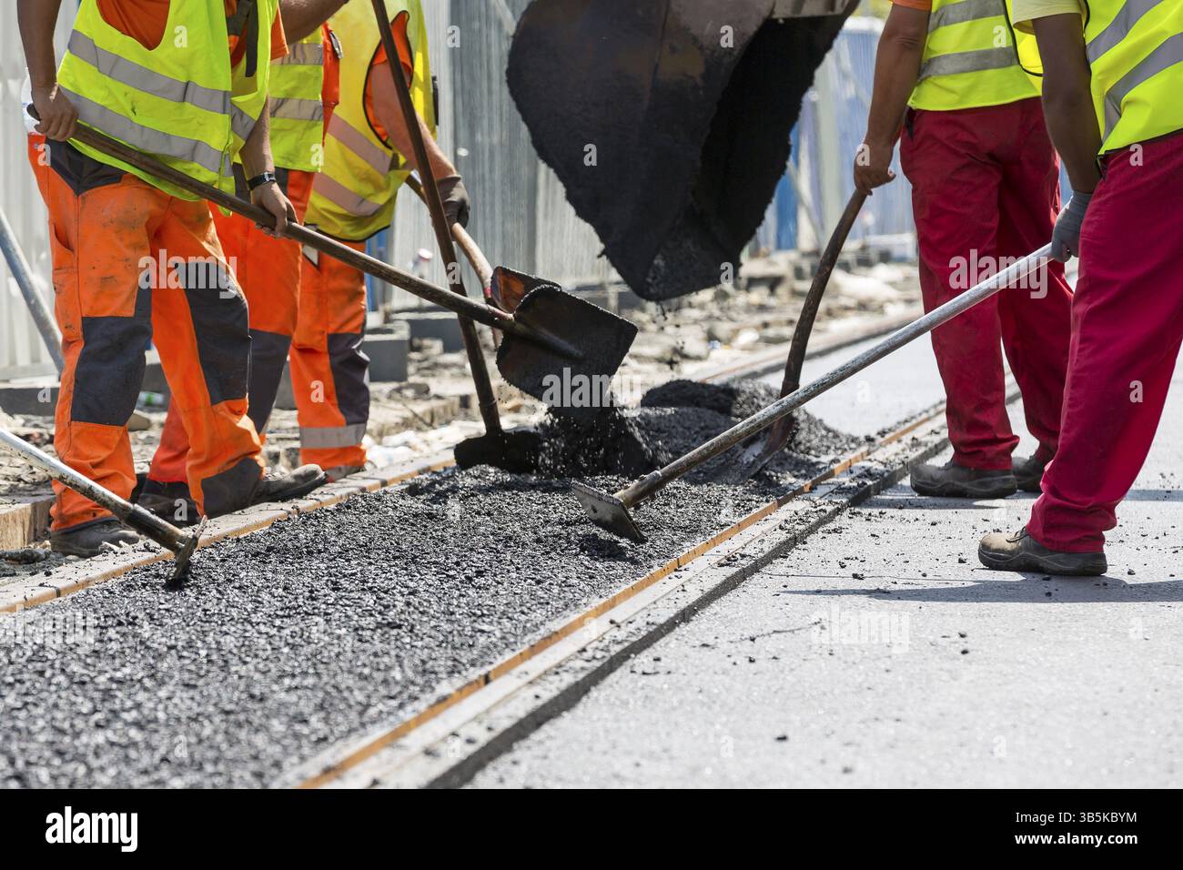Team of workers put the hot asphalt on a street along tram car's ...