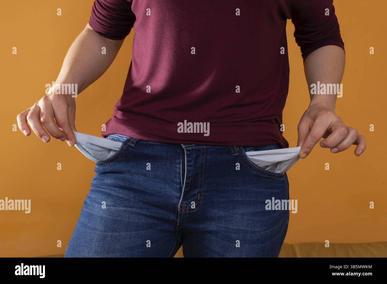 Empty pockets in blue jeans are shown by a young woman while facing the ...