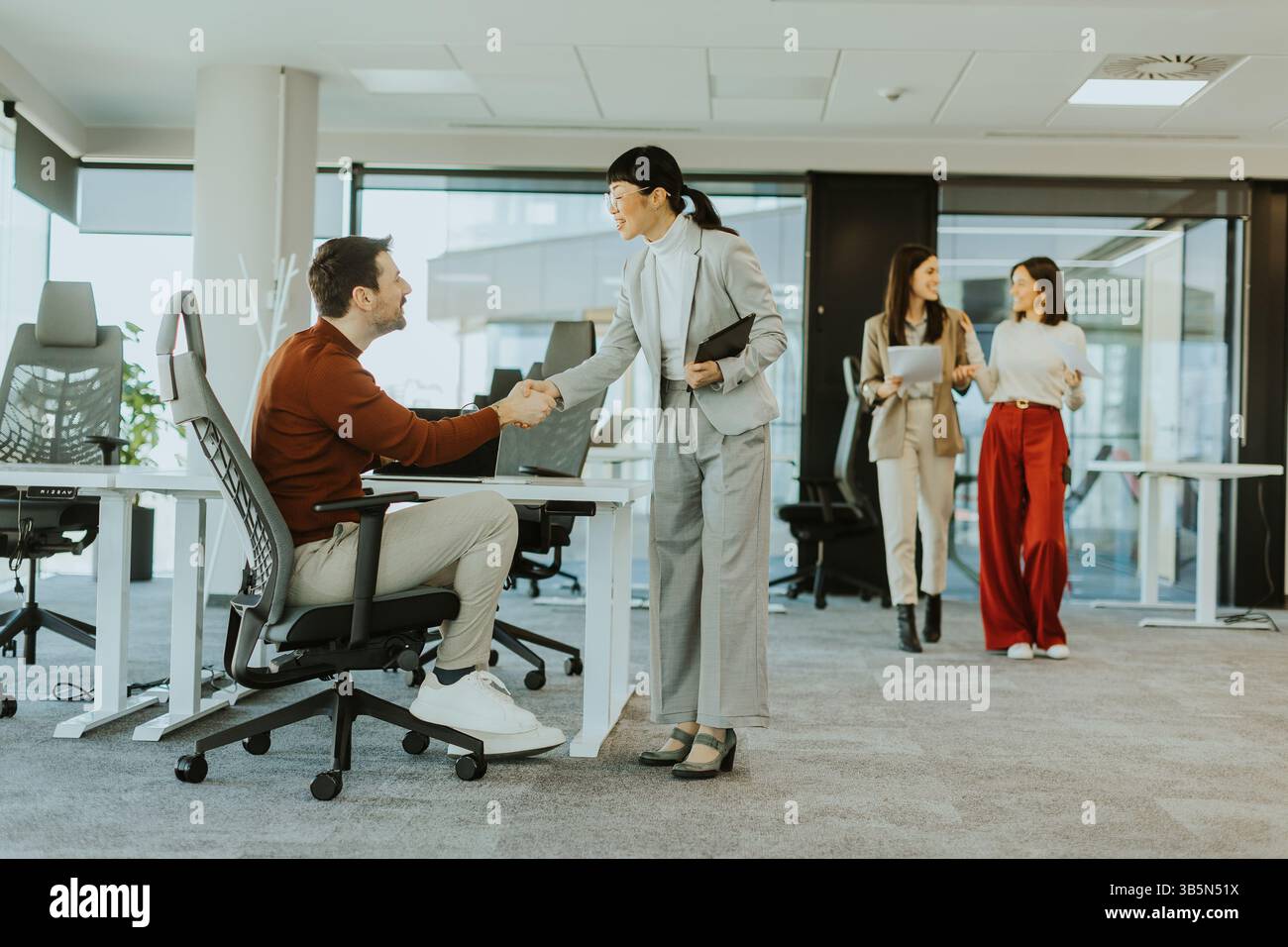 Bright office environment sees a joyful handshake between a male and ...