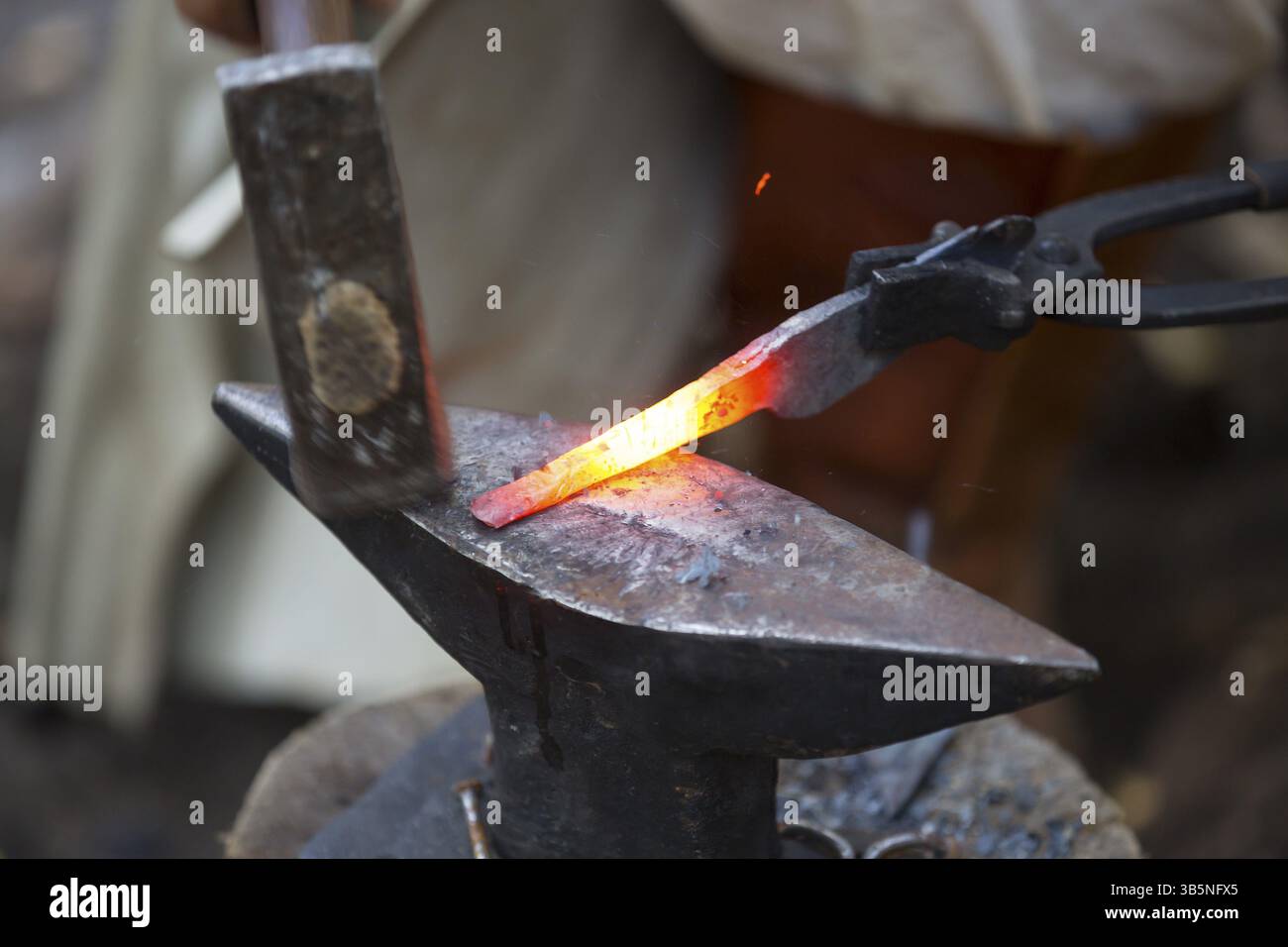 Blacksmith manually forging the molten metal. Blacksmith hammering hot ...