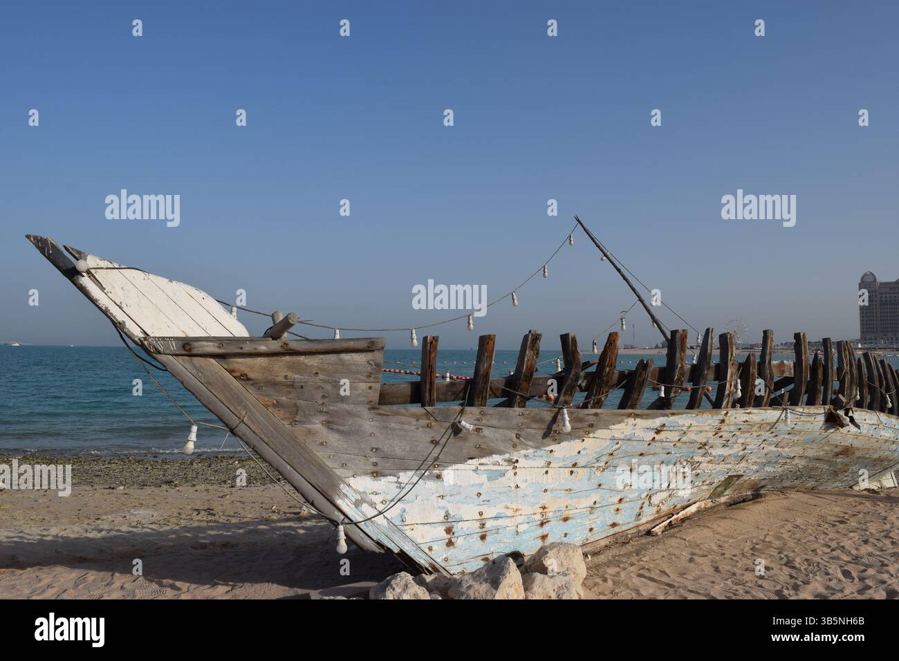 The skeletal remains of a weathered dhow boat lie tilted on the beach ...