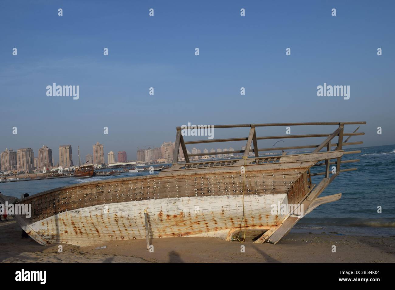 A traditional dhow boat under construction or restoration sits on the ...