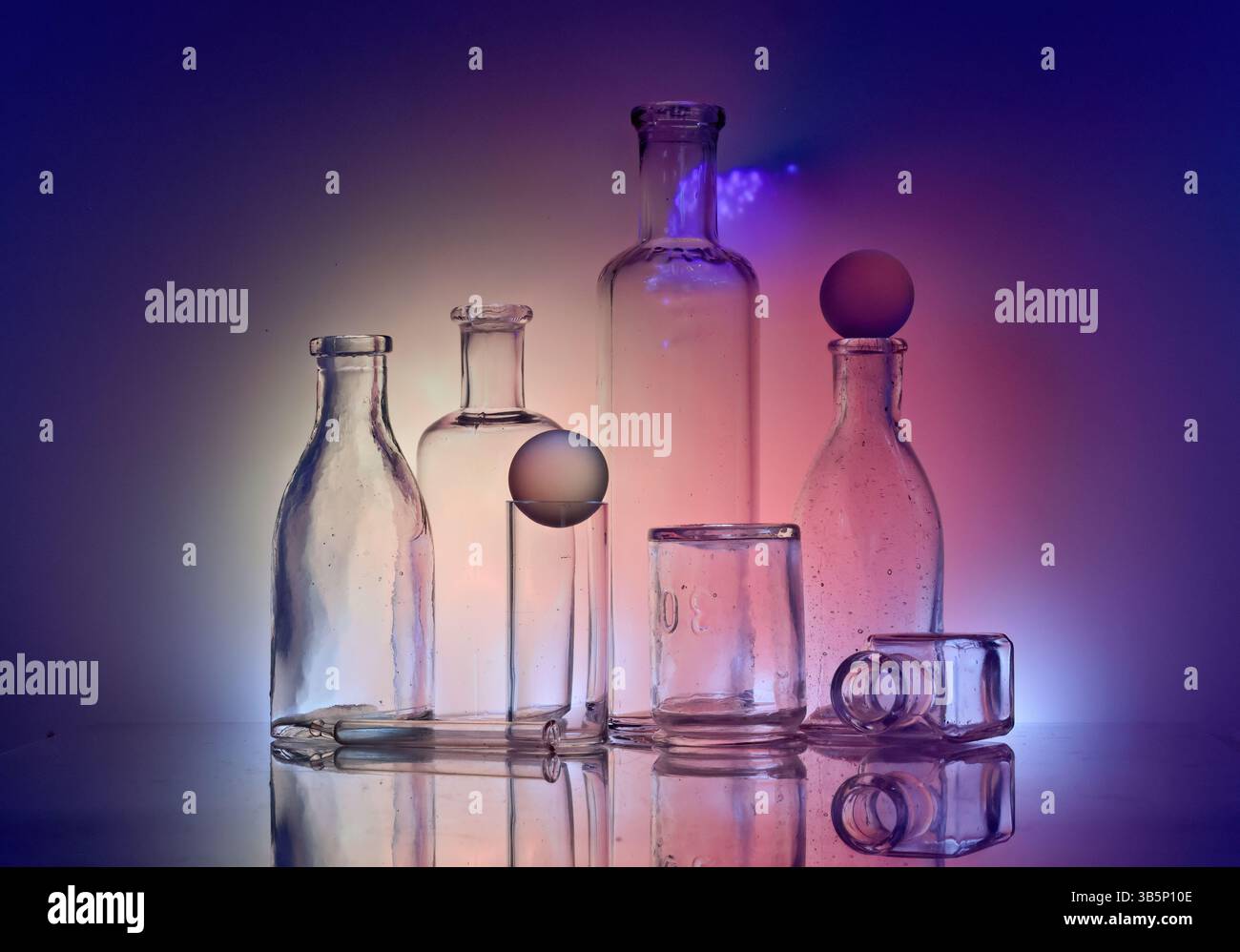 Old vintage glass bottles and jar on a reflective surface and colorful ...
