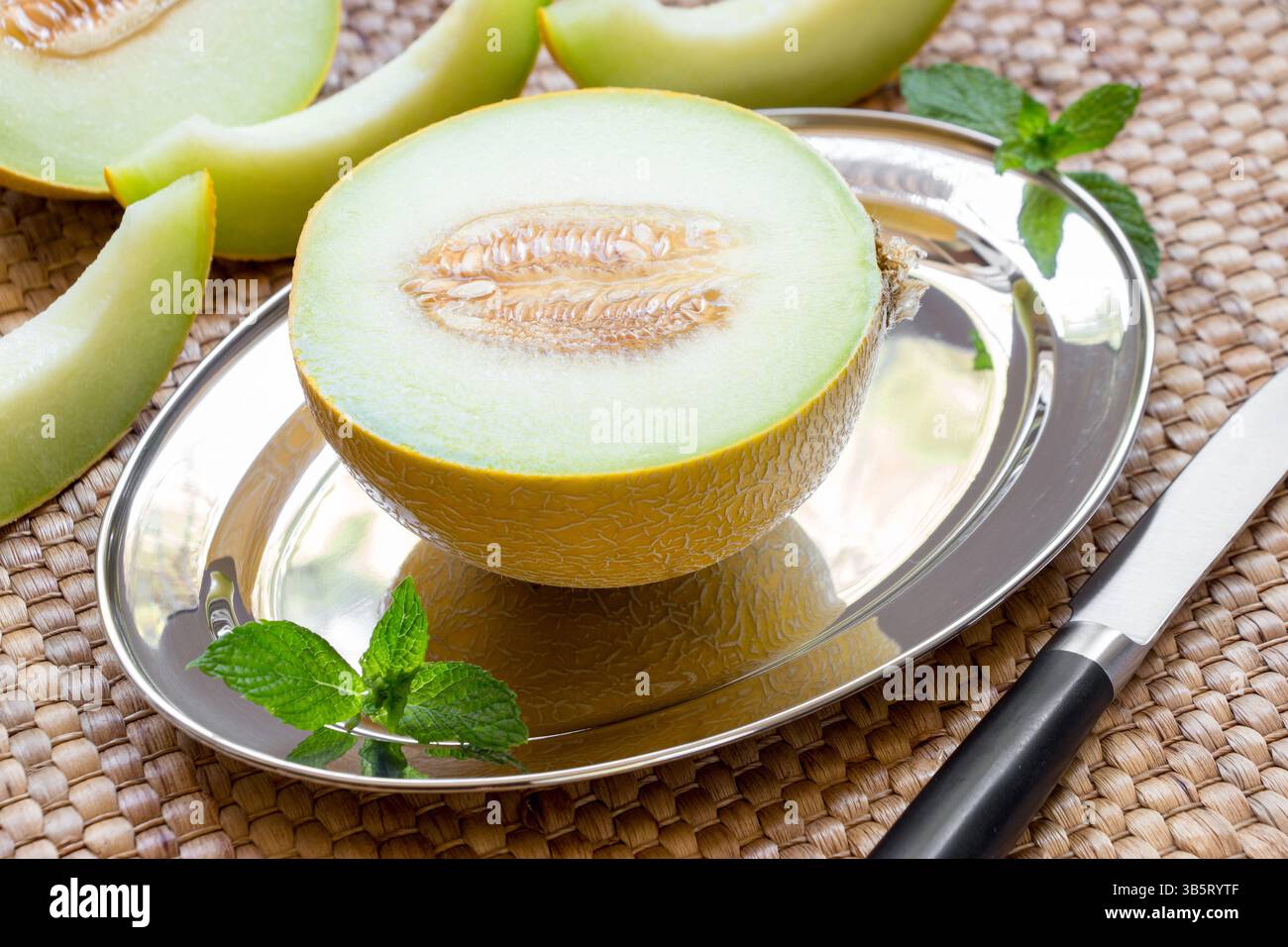 A perfectly halved honeydew melon displays its juicy interior on a shiny silver platter Stock ...