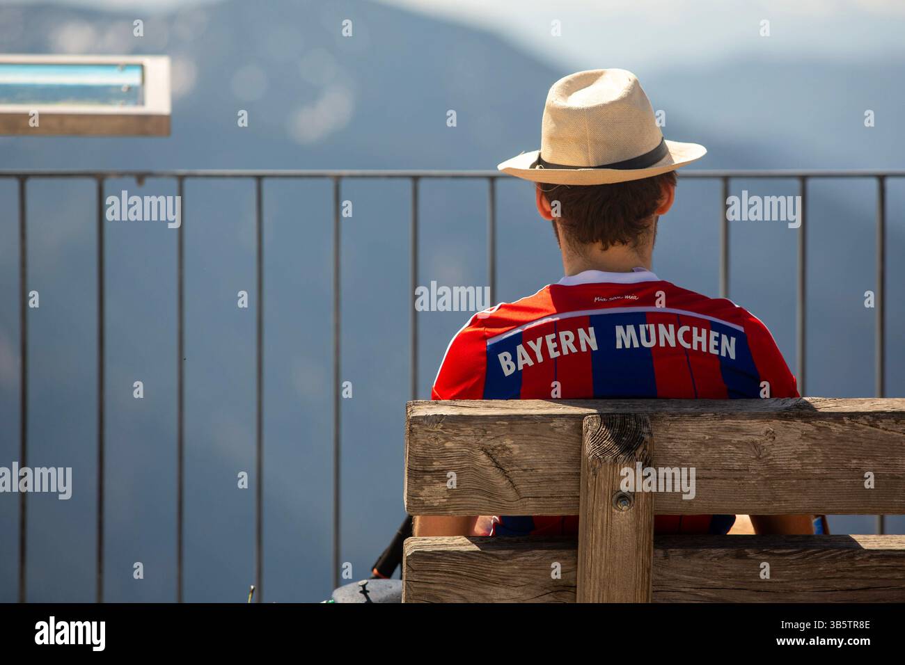 Ein Wanderer mit Hut und Trikot des FC Bayern München sitzt auf dem ...