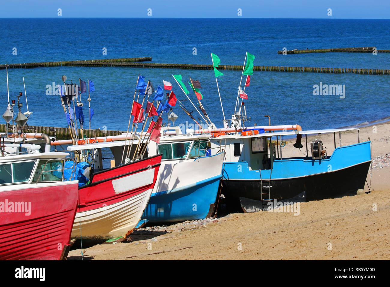 Colorful fishing boats with flags parked on a sandy beach by the Baltic ...