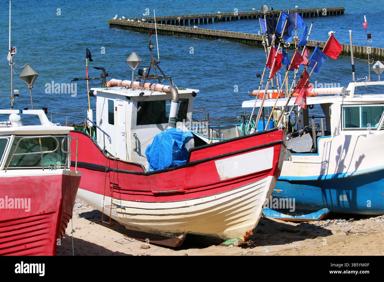 Colorful fishing boats with flags parked on a sandy beach by the Baltic ...