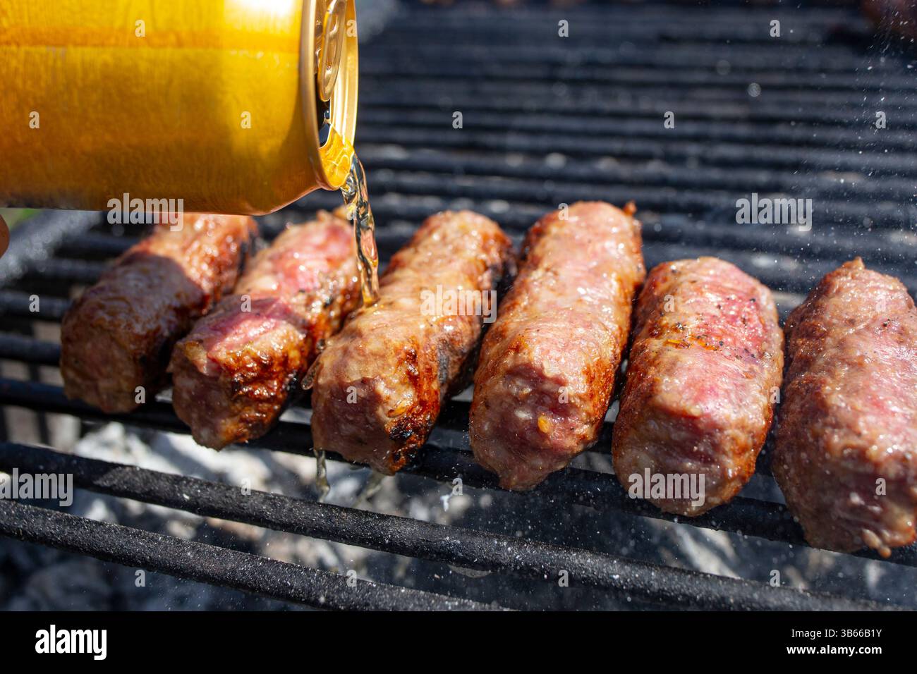 Pouring beer from a golden metal can on mici or mititei, Romanian traditional picnic food, on a ...