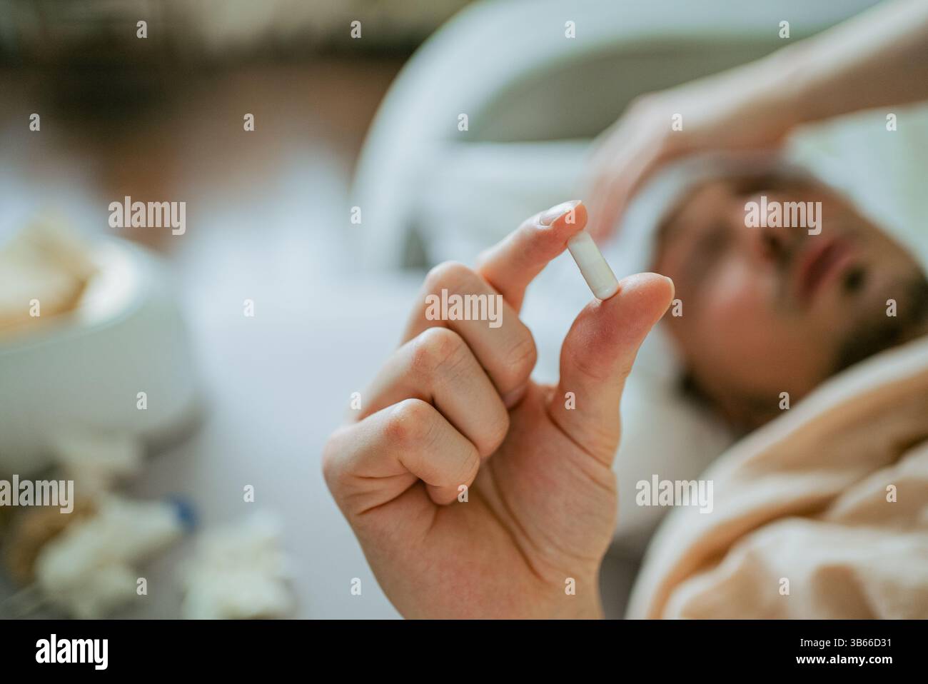 Sick man lying in bed, grasping a pill between his fingers, surrounded ...