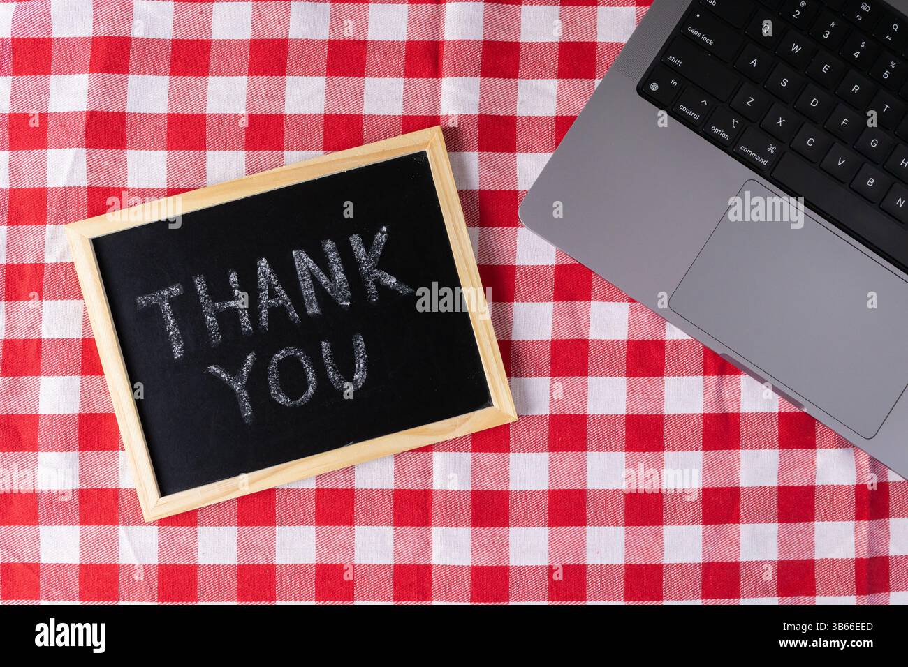 Small blackboard with Thank You message next to laptop on red checkered ...