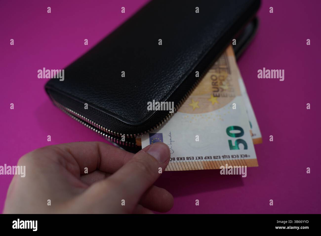 A hand pulling 50 euro banknotes from a black wallet on a pink ...