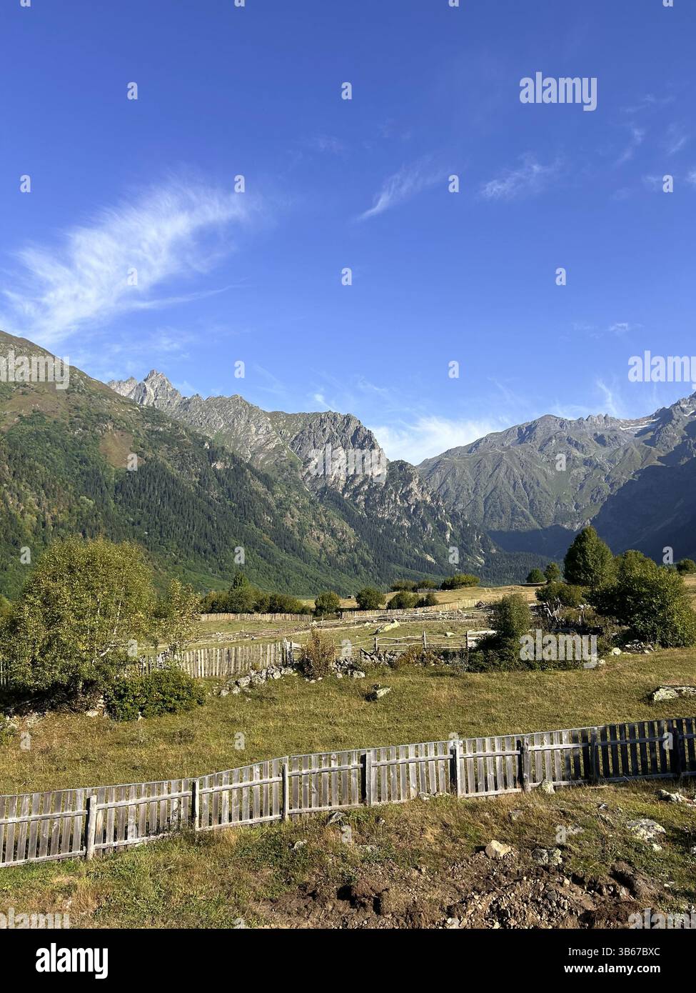 This image captures a wide mountain valley with grassy land, several ...