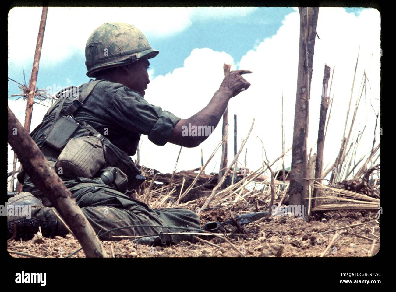 A Marine, under fire, points to an enemy position near the top of Hill ...