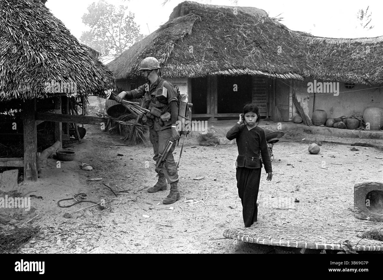 A Vietnamese woman walks through her village as a soldier sets fire to ...