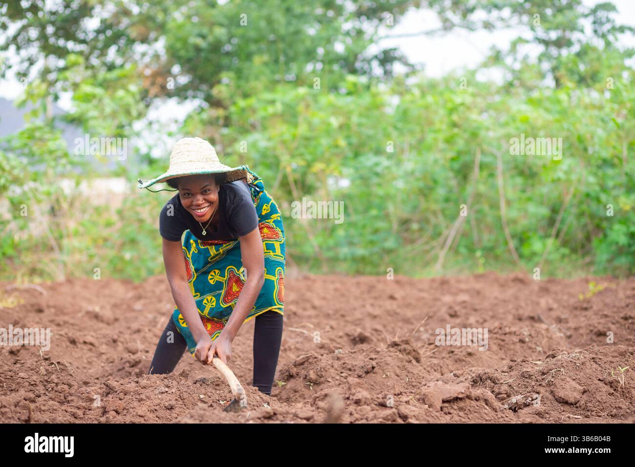 woman farmer working in a rural field, digging into the soil with a hoe ...