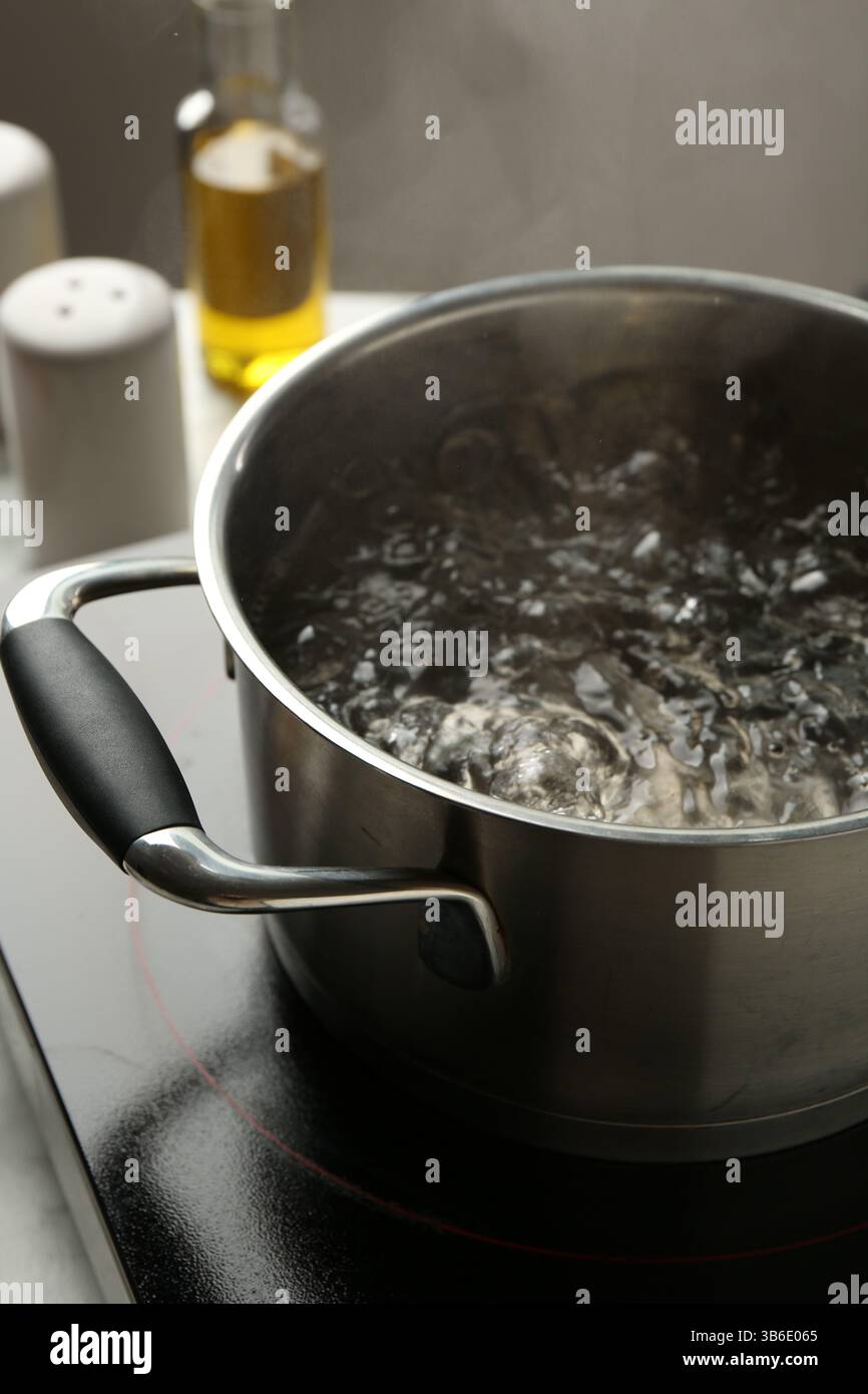 Cooking pot with boiling water and stove on table against grey ...