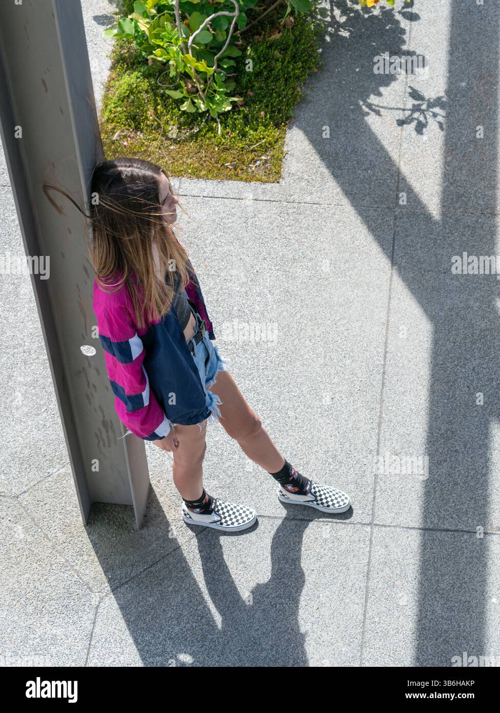 Teenage girl below standing leaning against post surrounded by shadows ...
