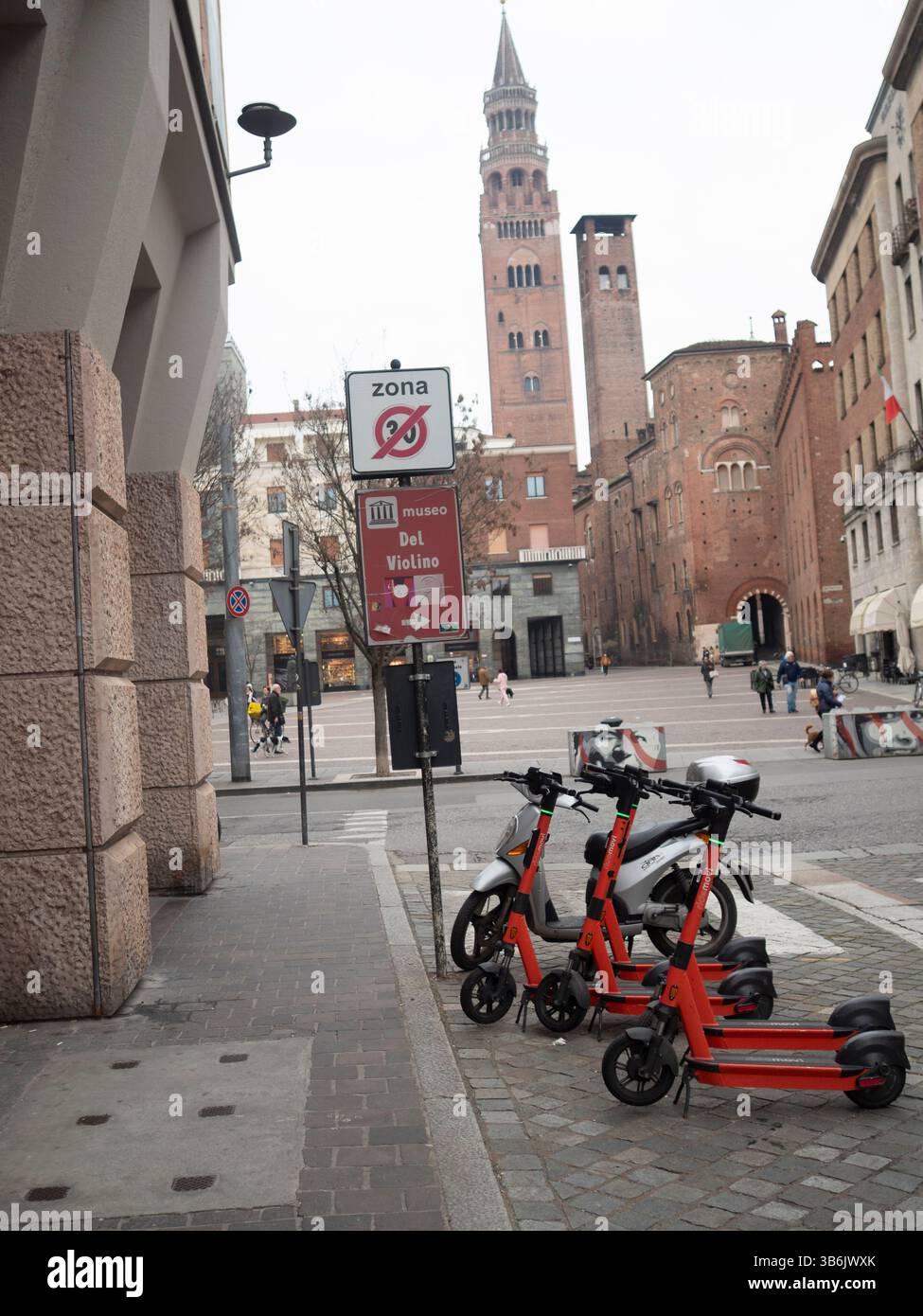 Cremona, Italy - April 12th 2025 Bright orange electric scooters for rent line a cobblestone ...