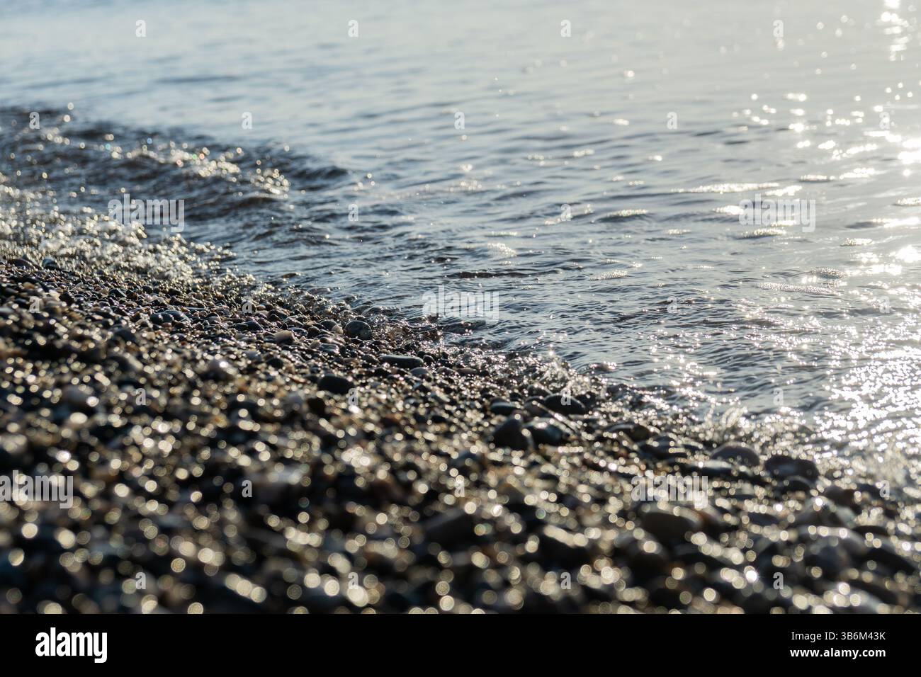 Gentle waves washing over smooth pebbles on a beach in the morning ...
