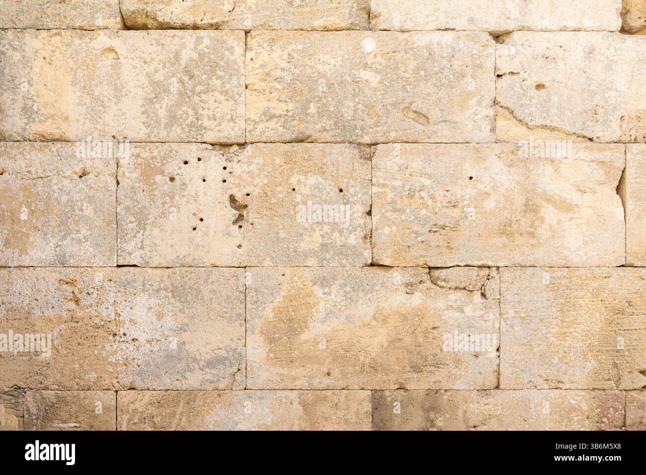 Rectangular blocks of beige limestone forming an old weathered wall ...